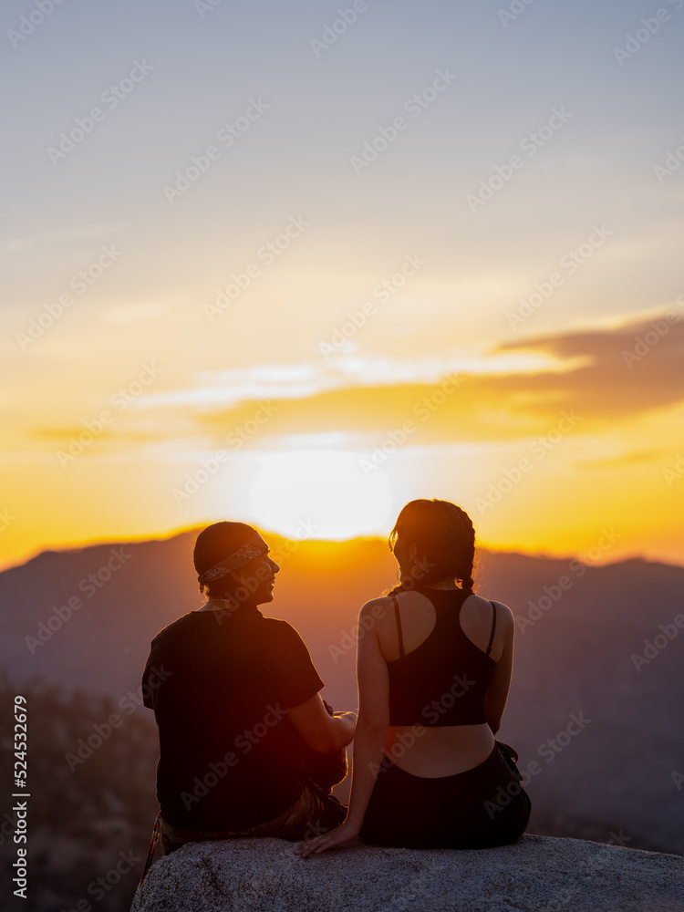 Young native friends sitting together on a mountain while the sun sets ...