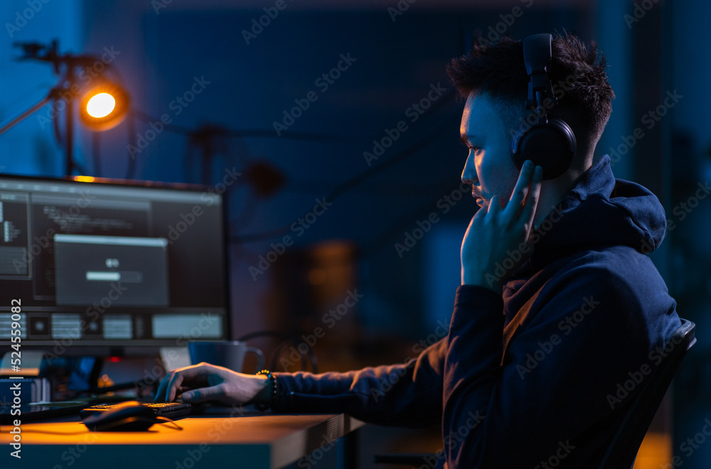 cybercrime, hacking and technology concept - male hacker in dark room writing code or using ...