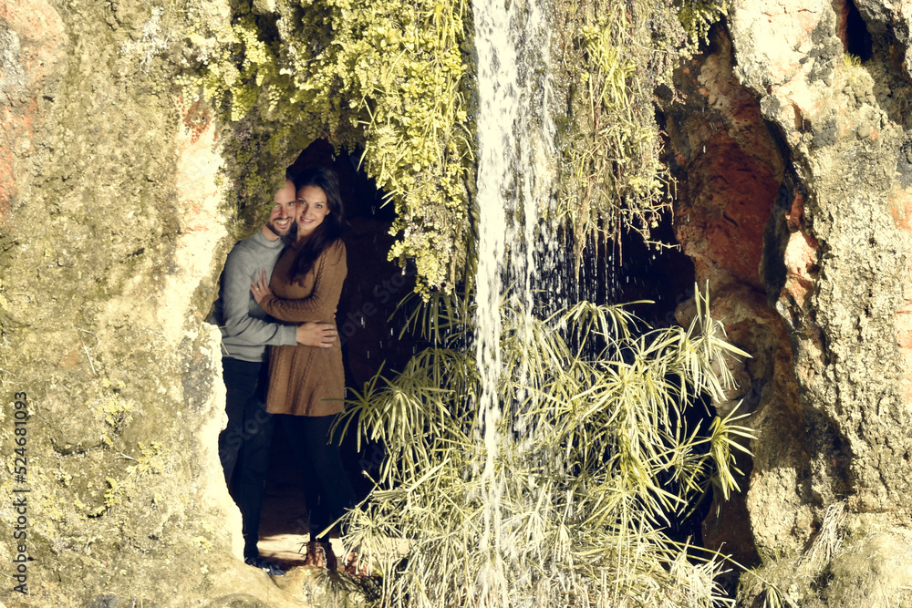 Pareja enamorados abrazados dentro de una cueva con una cascada de agua ...