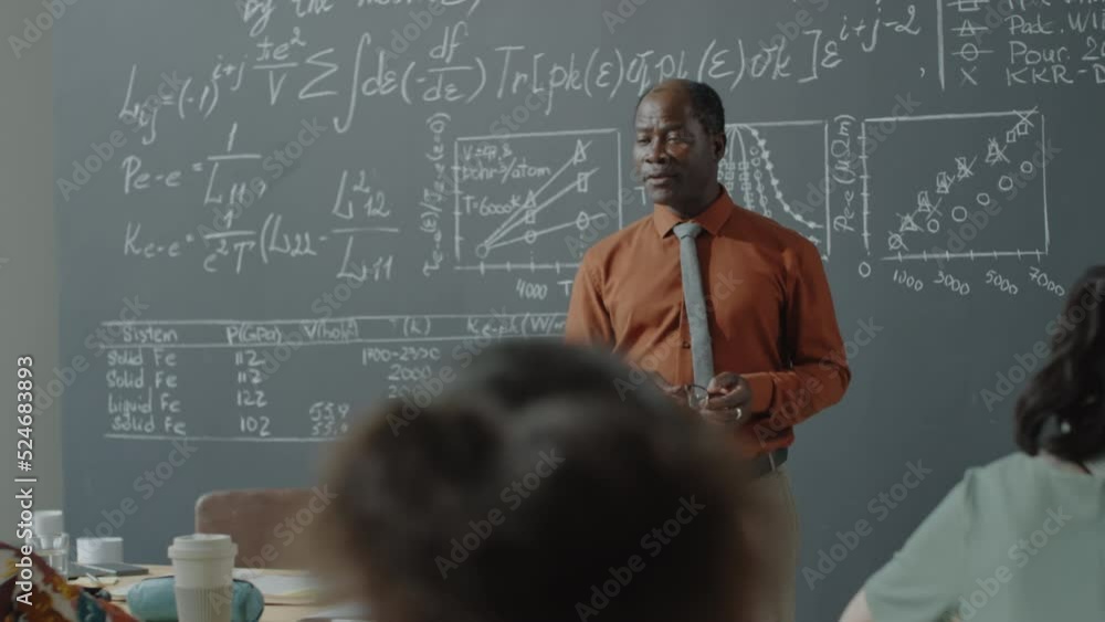 Mature African American professor standing by chalkboard in classroom ...