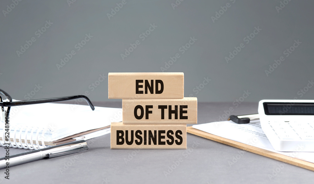 END OF THE BUSINESS text on a wooden block with notebook,chart and ...