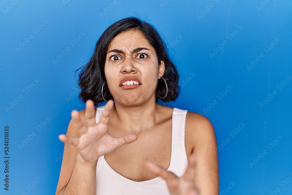 Young hispanic woman standing over blue background disgusted expression ...