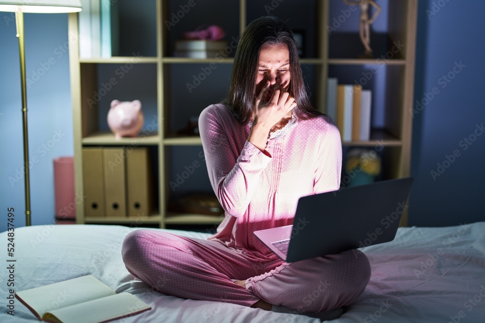 Young hispanic woman using computer laptop on the bed smelling ...
