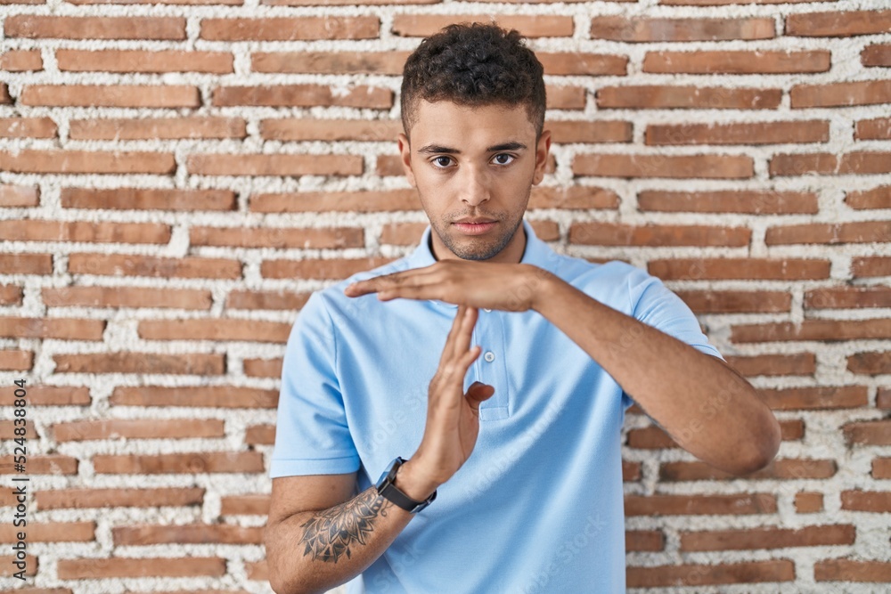 Brazilian young man standing over brick wall doing time out gesture ...
