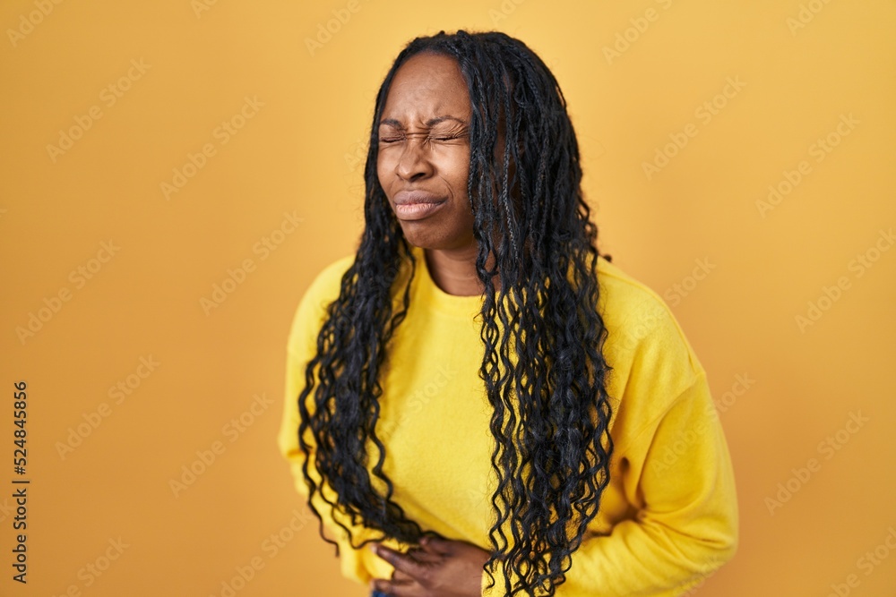 African woman standing over yellow background with hand on stomach ...