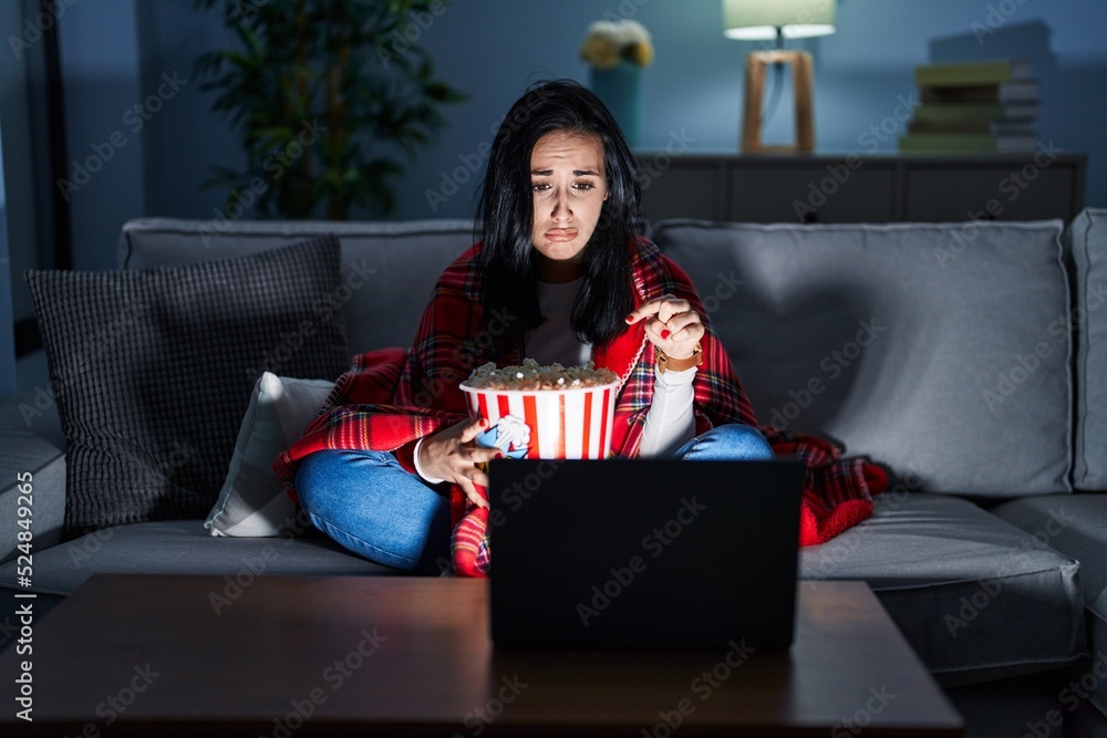 Hispanic woman eating popcorn watching a movie on the sofa pointing ...