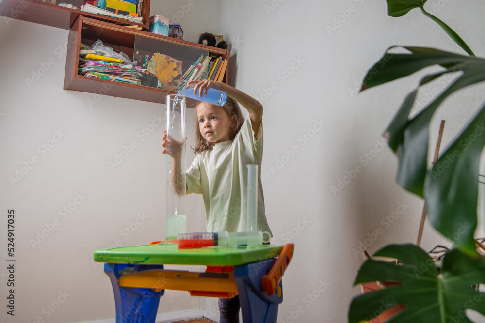 Kid pours a colored liquid into a test tube while making a chemistry ...