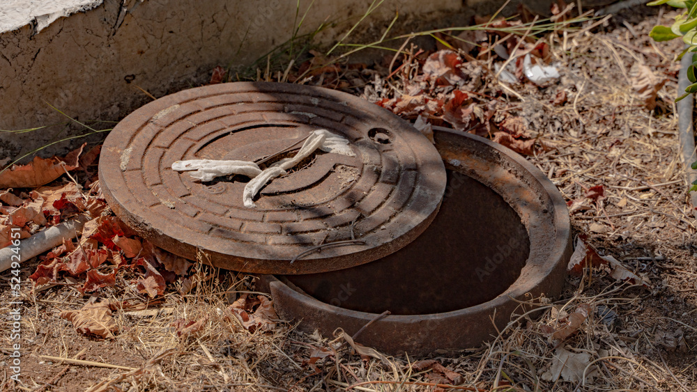 an open sewer manhole rusted with time and water against a backdrop of ...