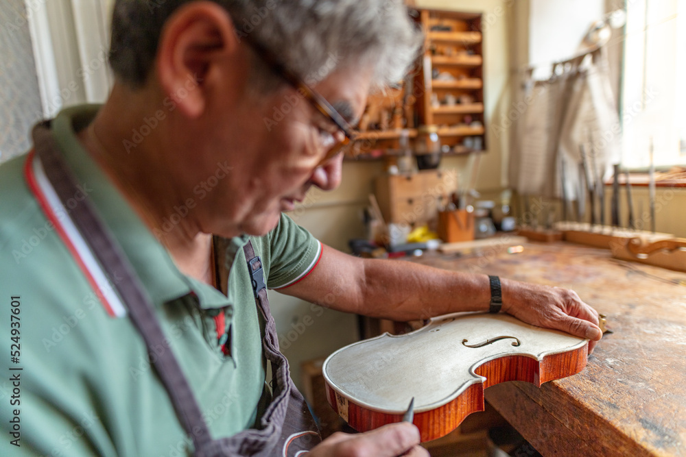 luthier carving the shape of the outside of the front of a violin with ...