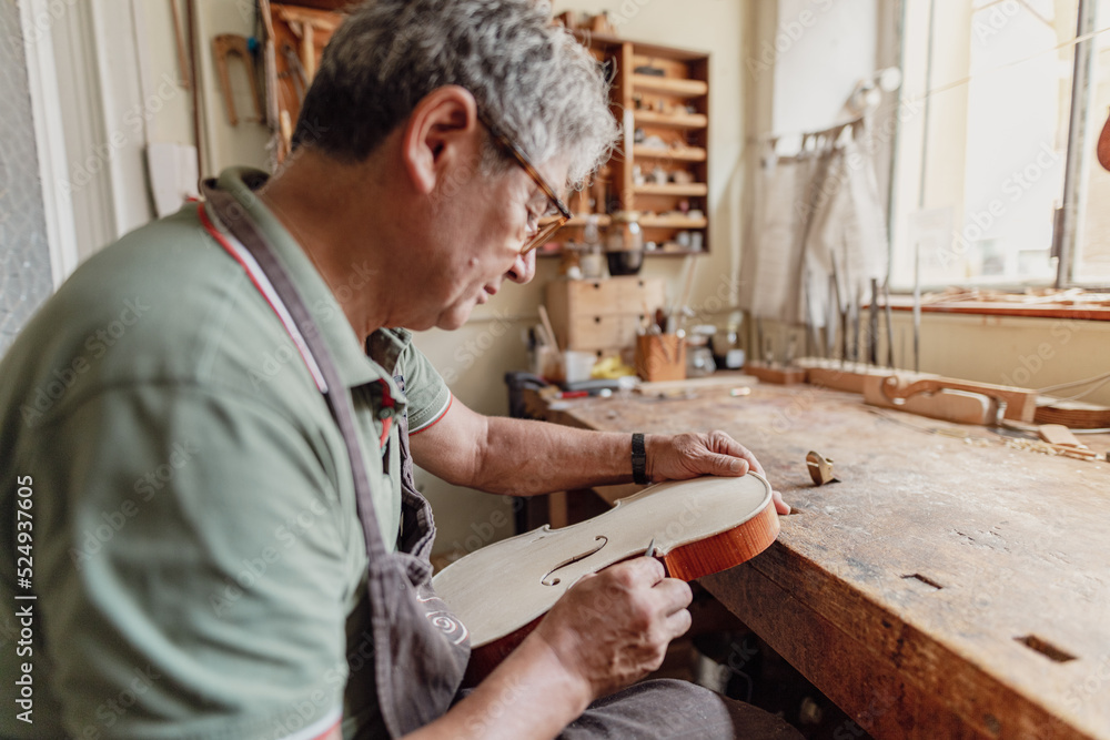 luthier carving the shape of the outside of the front of a violin with ...