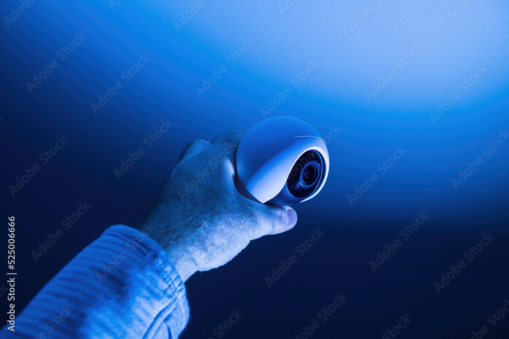 Blue color cast over male hand holding modern tiny 8k UHD surveillance ...