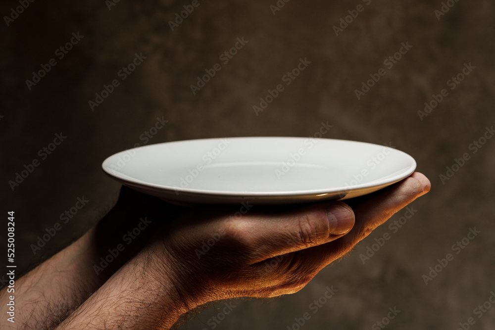 Male hands holding empty plate on dark background, lack of food, hunger ...