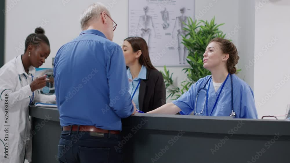 Medical assistant giving support to old patient at reception desk in ...