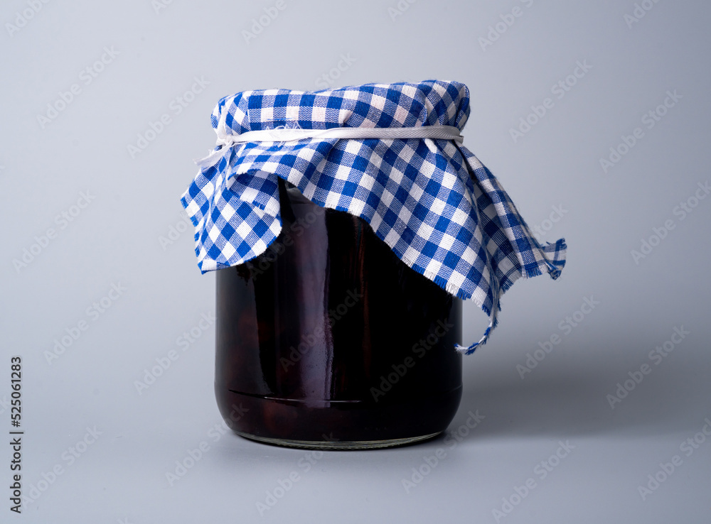 Glass jar with red jam decorated with blue and white checkered cloth on ...