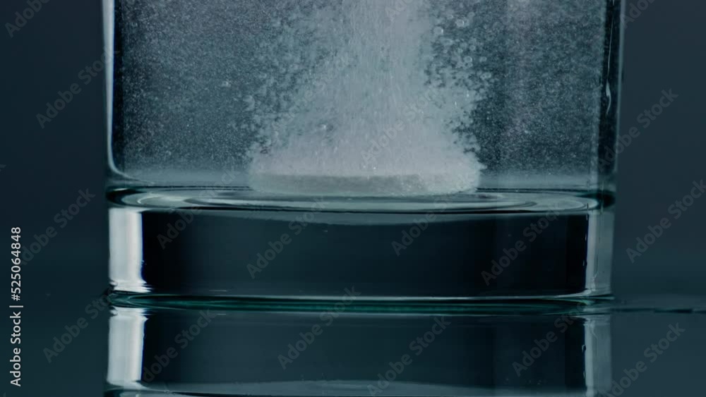White tablet dissolving water in transparent cup closeup. Fizzy pill ...