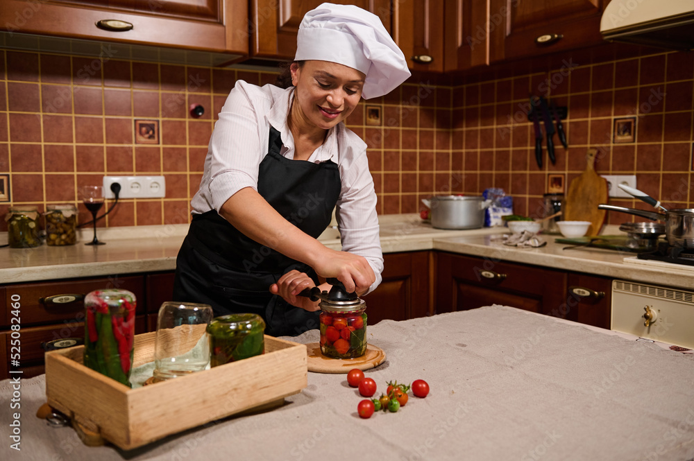 Delightful multi-ethnic young woman, housewife wearing white chef's cap ...