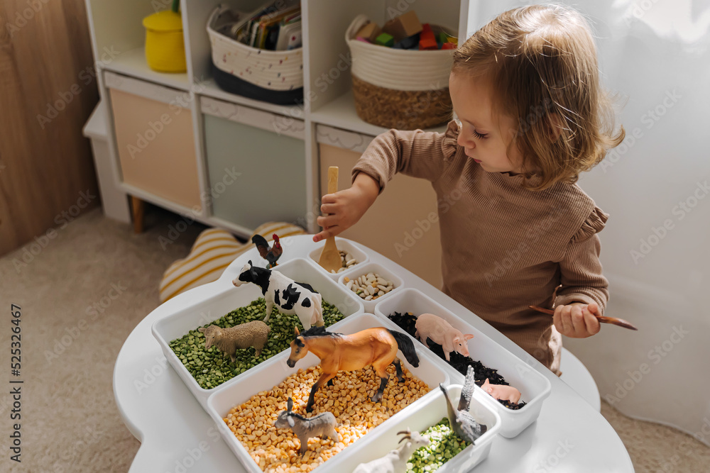 A little girl playing with farm animals in sensory bin in nursery ...