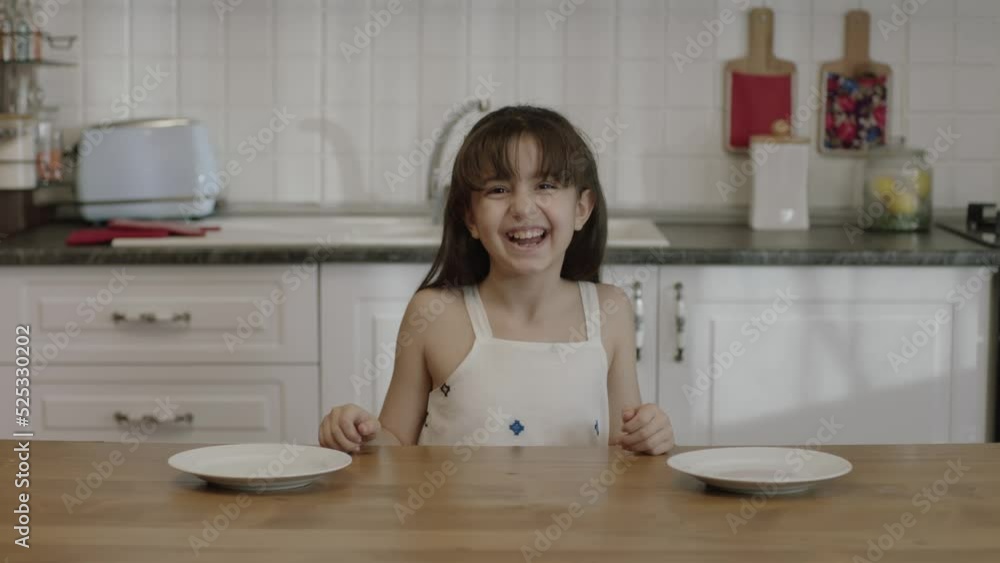Cute little girl is waiting for her food at the kitchen table. She is ...