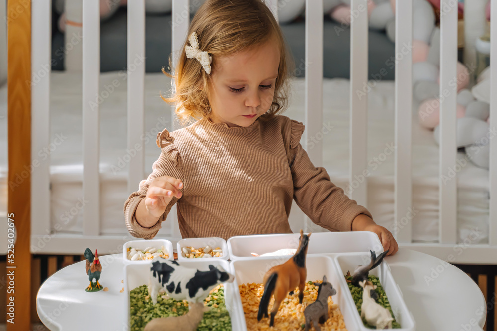 A little girl playing with farm animals in sensory bin in nursery ...