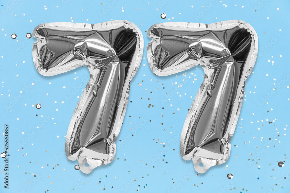 Silver foil balloon number, digit seventy seven on a blue background ...