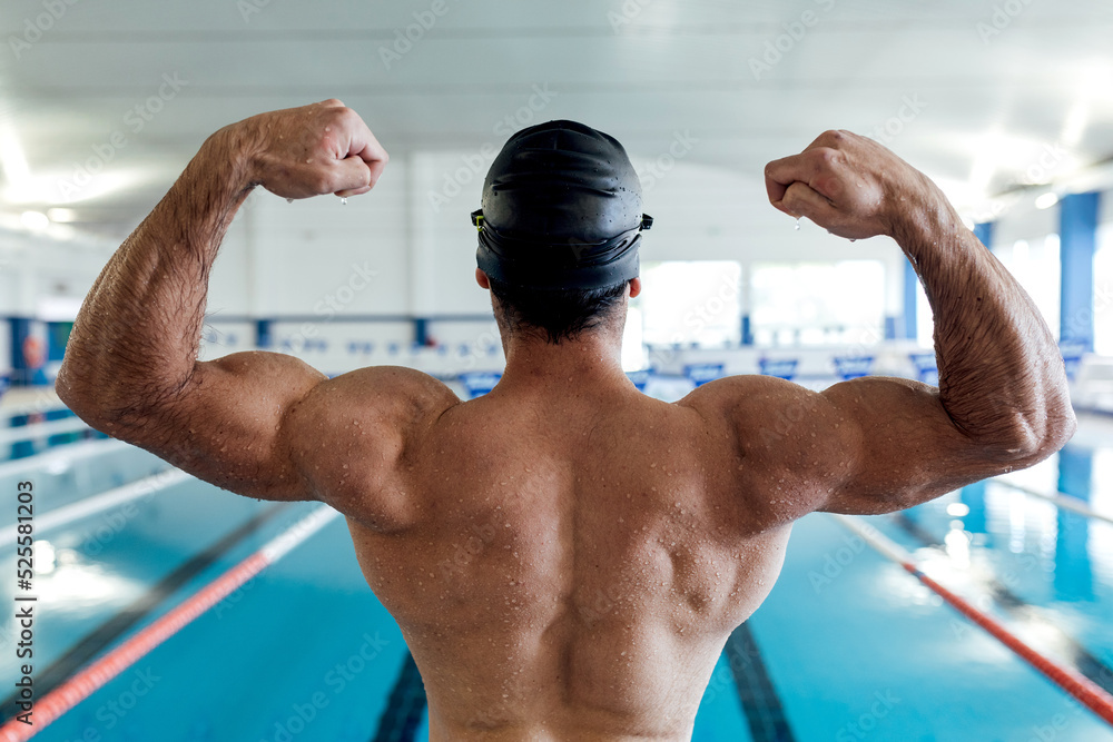 Unrecognizable muscular swimmer showing biceps against pool indoors ...
