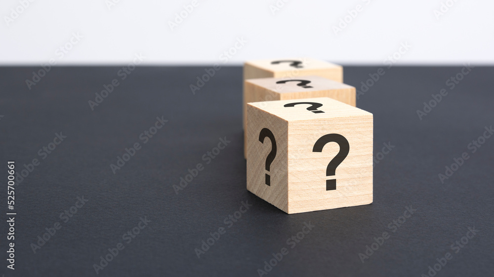 staggered row of three wooden blocks with question marks on black table ...