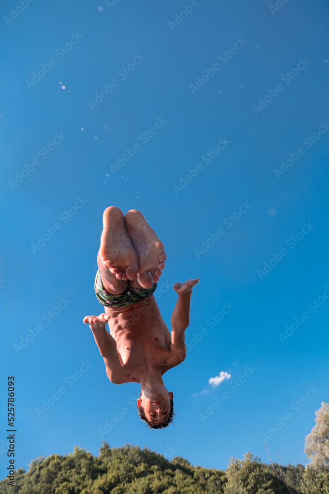 Young teen boy jumping flying and diving in the river. Clear blue sky ...