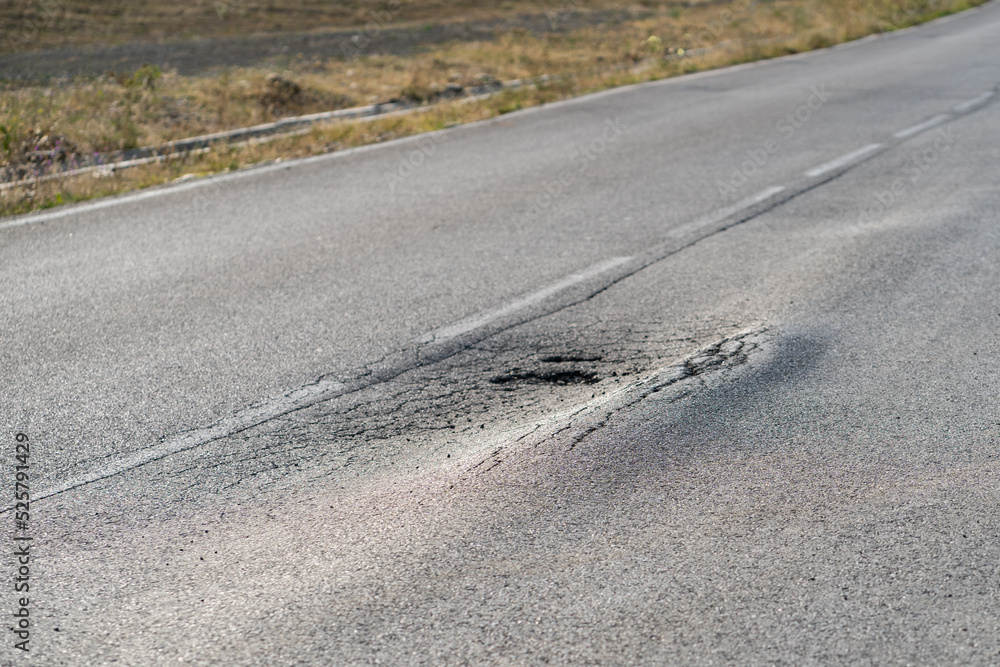 Broken road with holes and cracks built in countryside on hot sunny day ...
