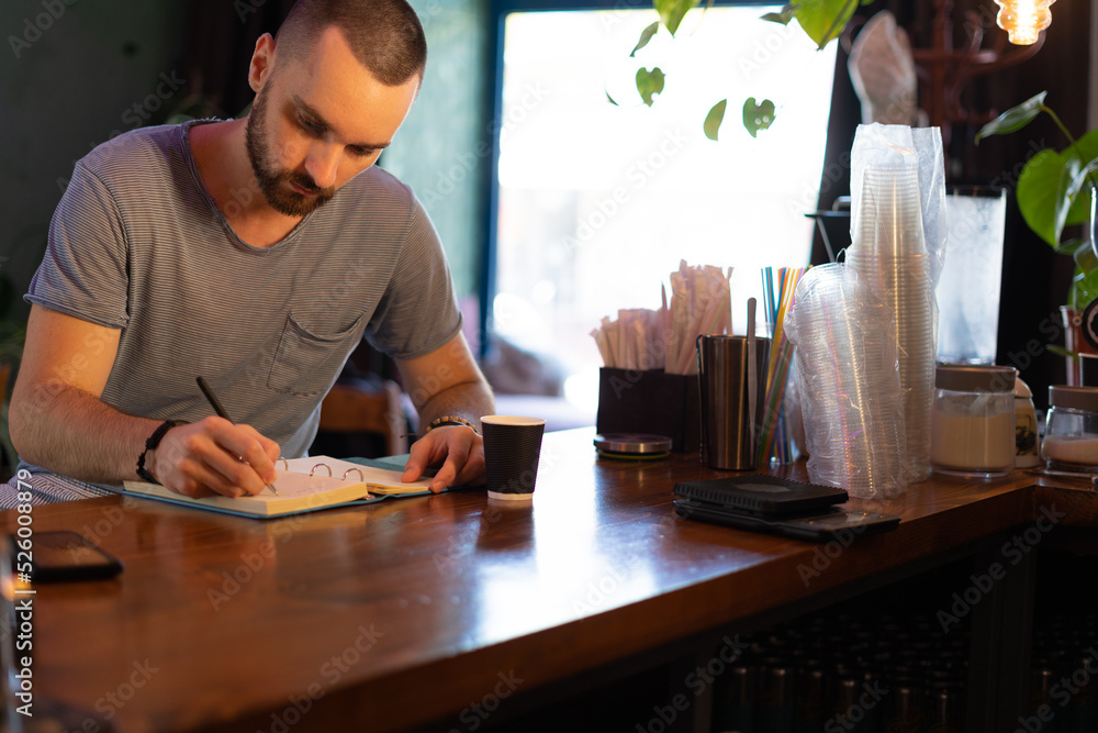 Young bar owner standing at bar counter thinking writing receipt in ...