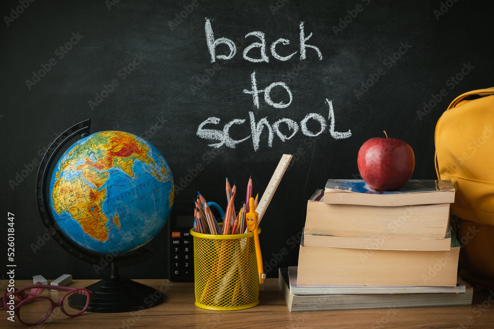 School supplies next to the globe and stack of books on the blackboard ...