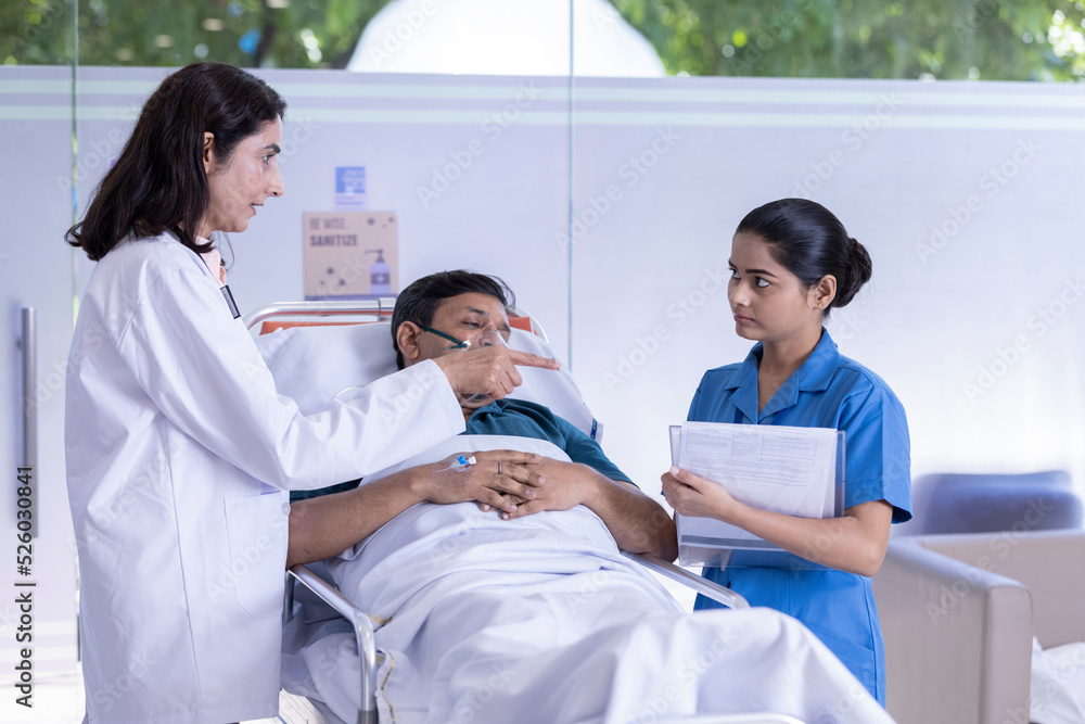 Female doctor scolding nurse with report while patient is lying on ...
