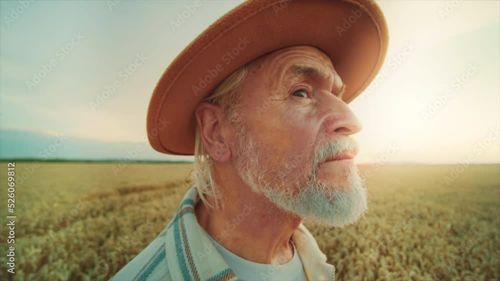 Portrait of elderly white-haired Caucasian farmer in hat looking around ...