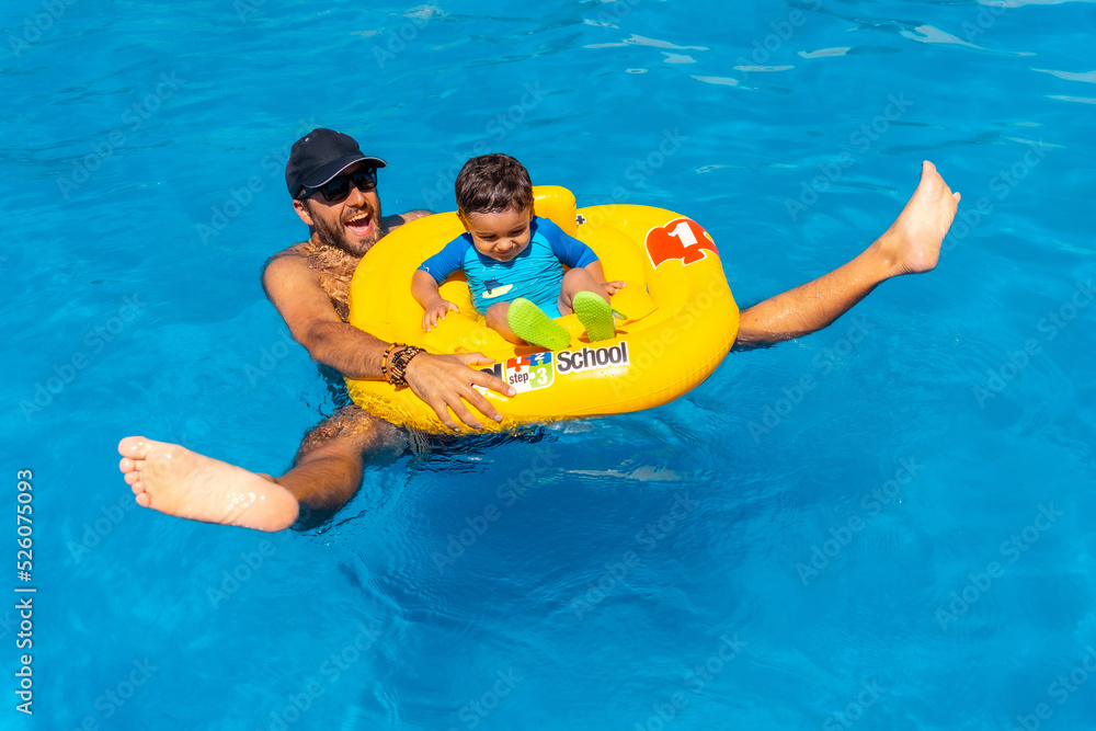 Father playing with his son with a yellow float in the pool in summer ...