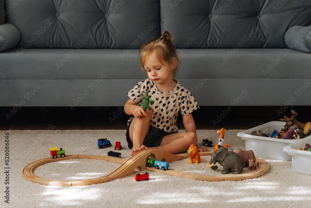 Kid girl builds a toy town and wooden railway. A little girl sitting on ...