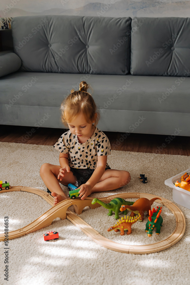 Kid girl builds a toy town and wooden railway. A little girl sitting on ...