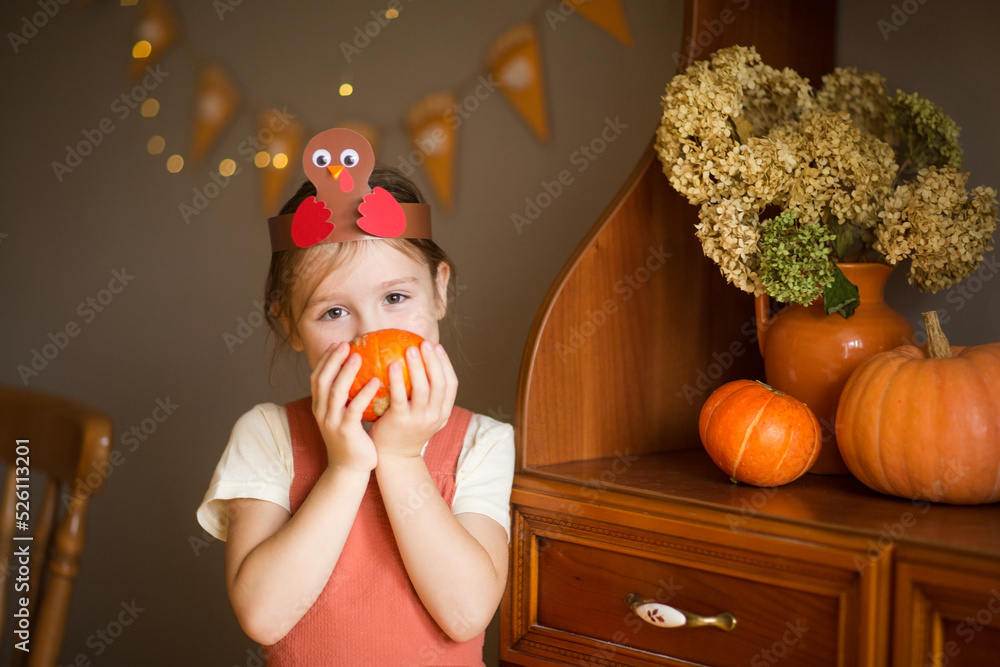 child in headdress in form of turkey with large pumpkin on background ...