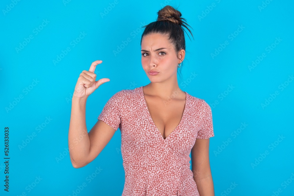 Displeased beautiful brunette woman wearing floral dress over blue ...