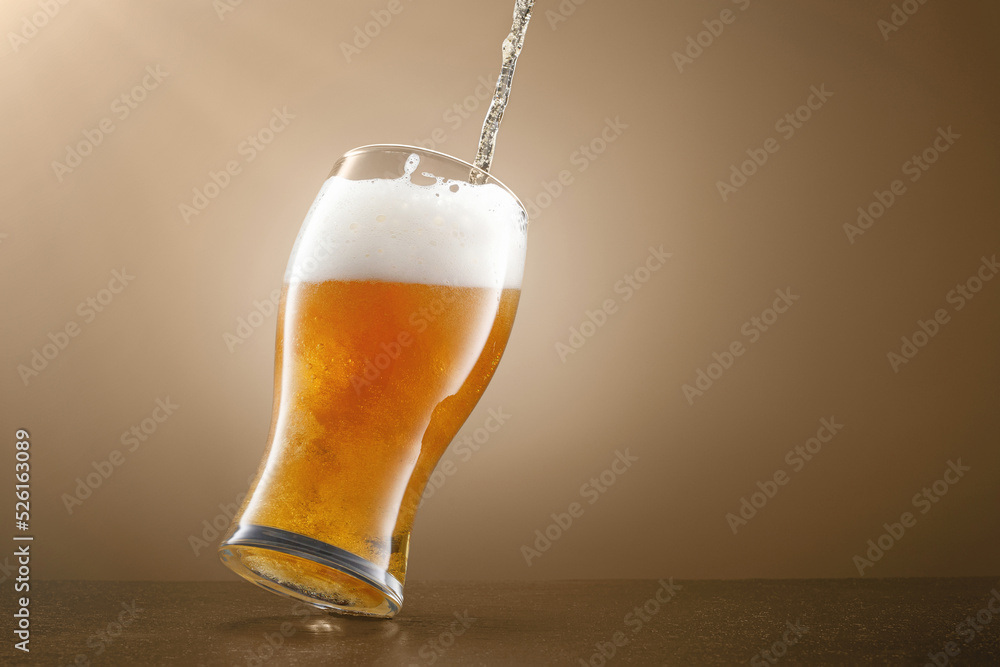 Stream of draught beer in glass on a beige background. Pouring lager ...