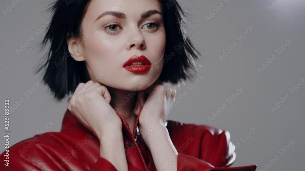 A woman with beautiful makeup and red lips poses in a red coat close-up ...