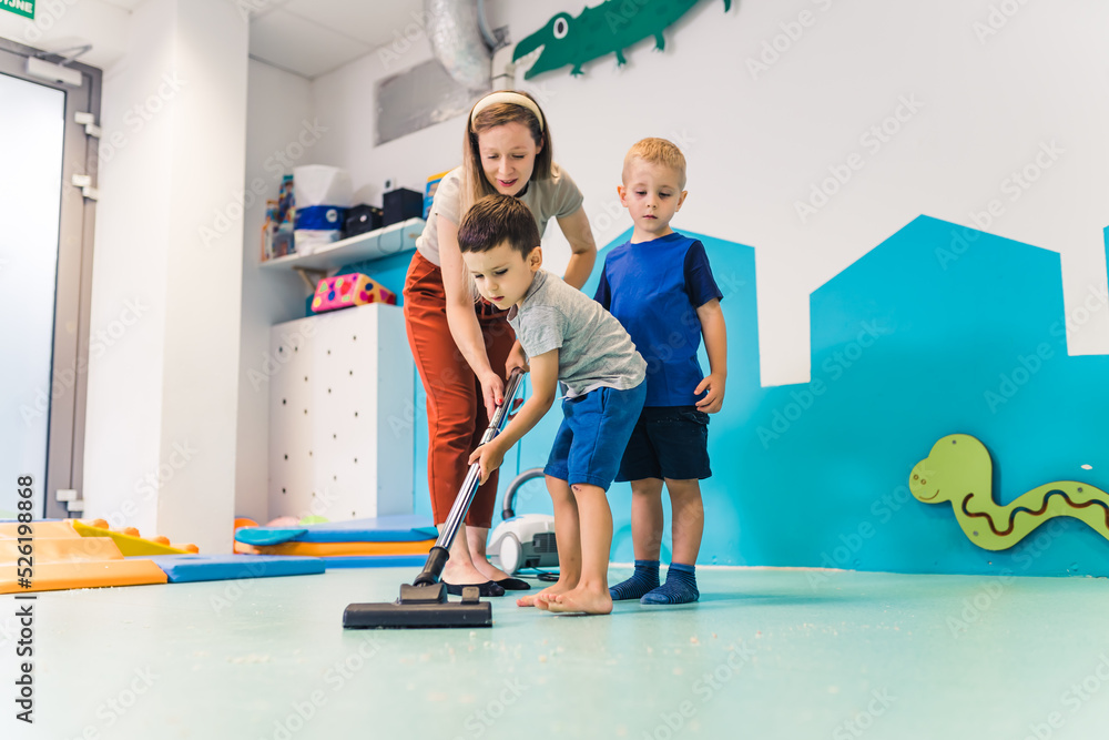 Little helpers, toddlers boys vacuuming, helping their teacher to clean the room after play at ...