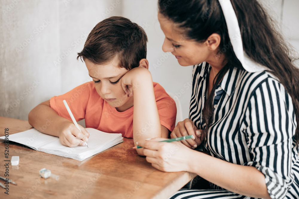 Little school boy doing homework with his mom helping him with ...
