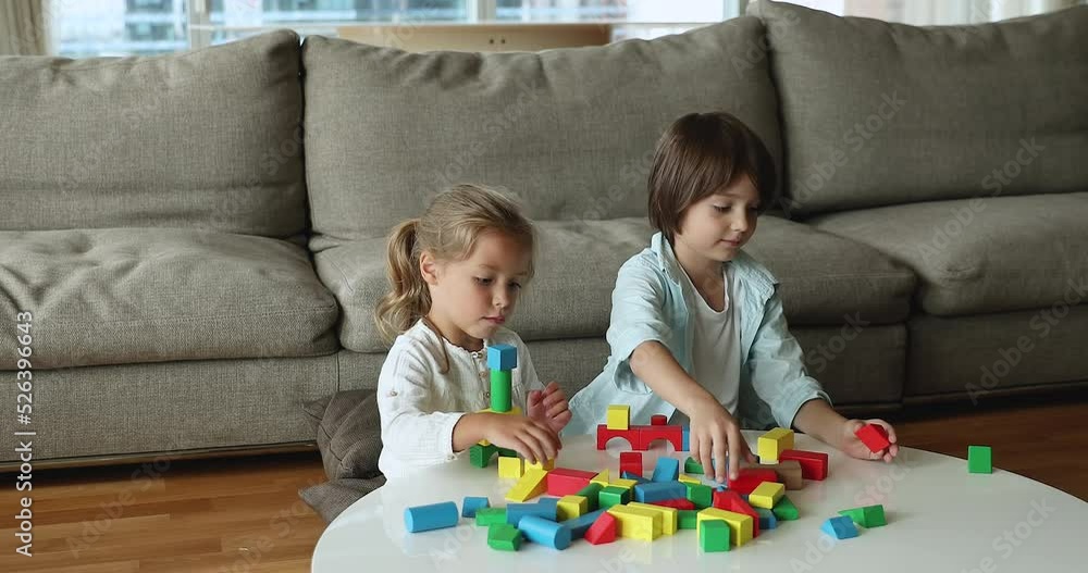 Two focused cute sibling kids playing building blocks at home, stacking ...