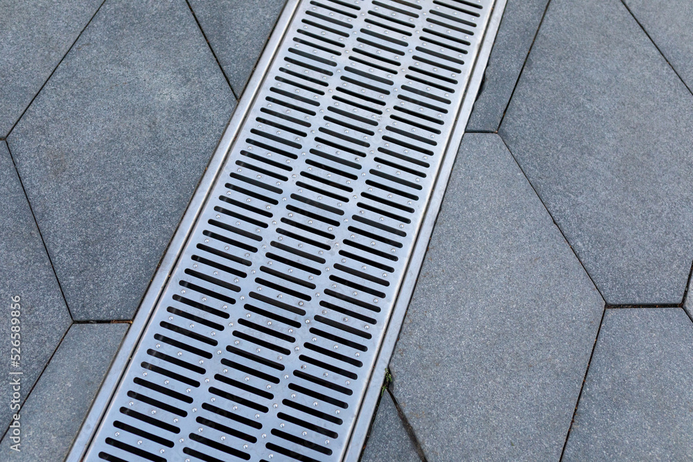 Metal storm sewer grate on shaped paving slabs in park. Drainage ...