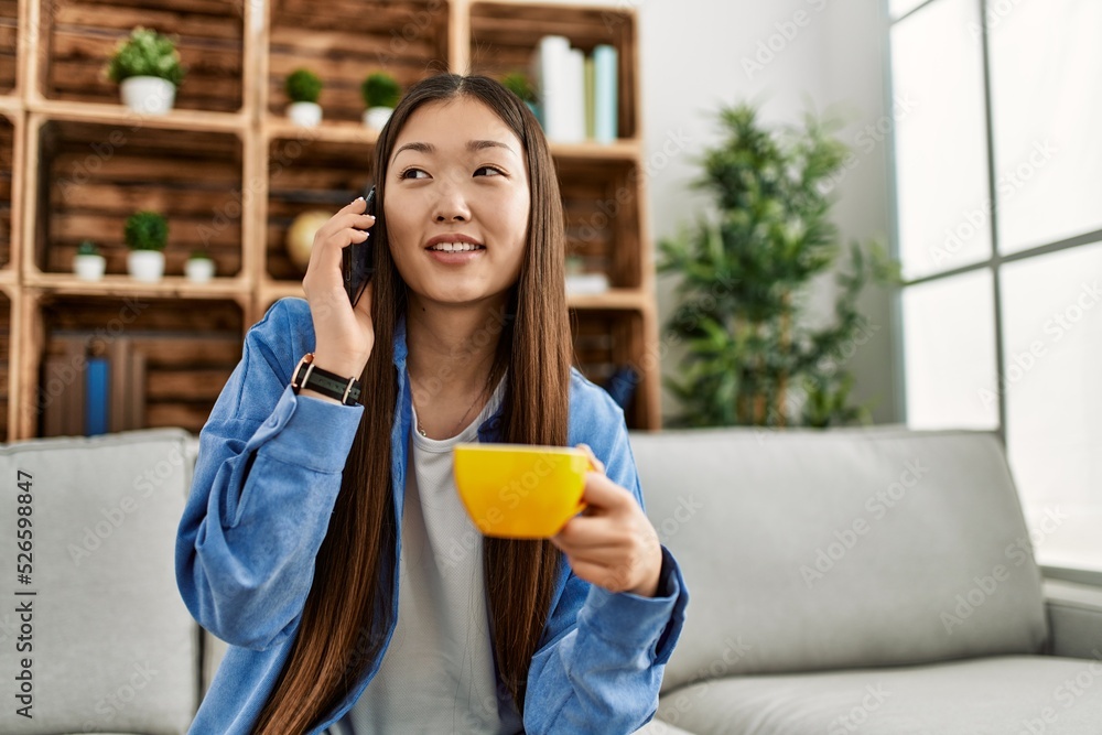 Young chinese girl talking on the smartphone and drinking coffee ...