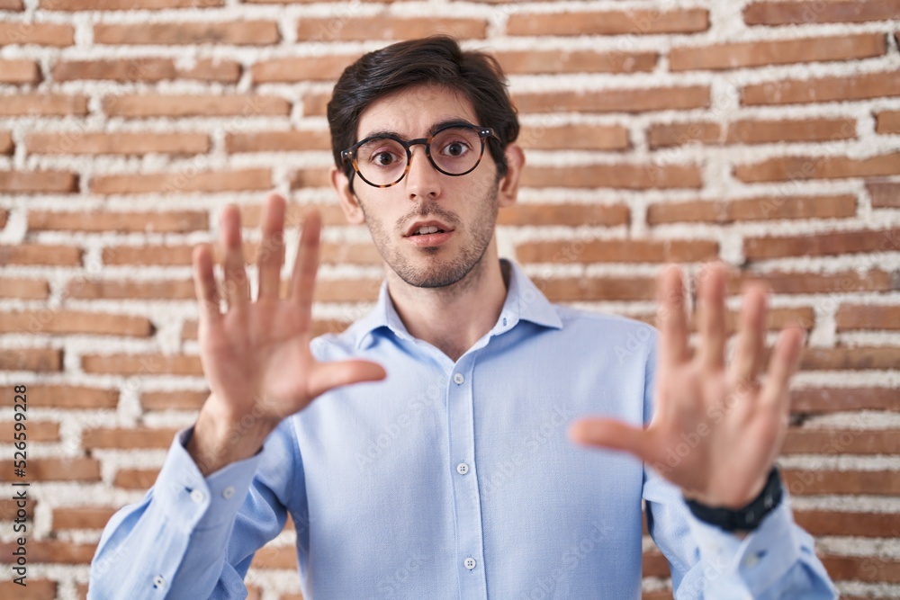 Young hispanic man standing over brick wall background afraid and ...