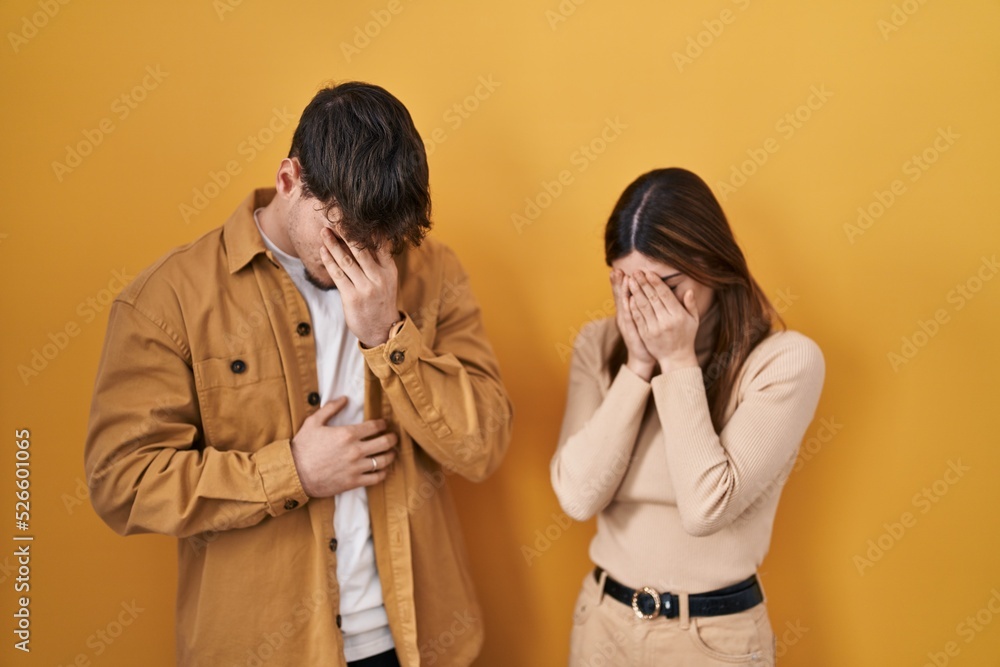 Young hispanic couple standing over yellow background with sad ...