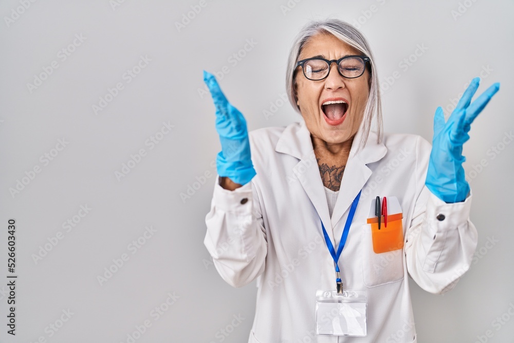 Middle age woman with grey hair wearing scientist robe celebrating mad ...