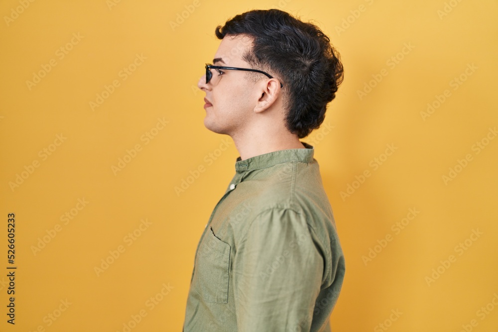 Non binary person standing over yellow background looking to side ...