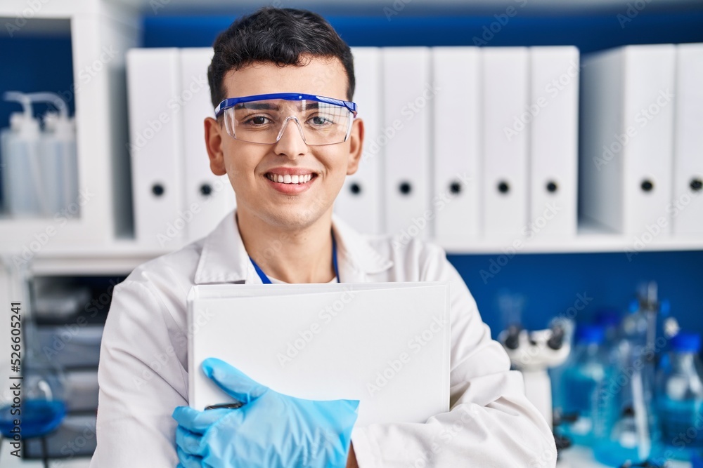 Young non binary man scientist smiling confident hugging binder at ...