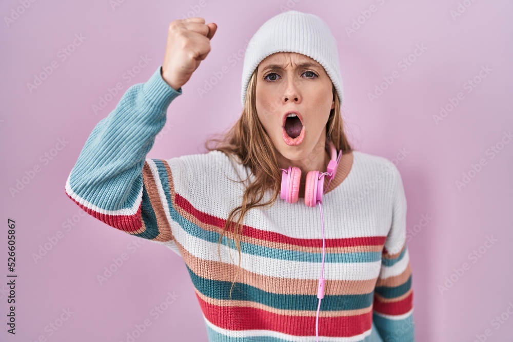 Young blonde woman standing over pink background angry and mad raising ...